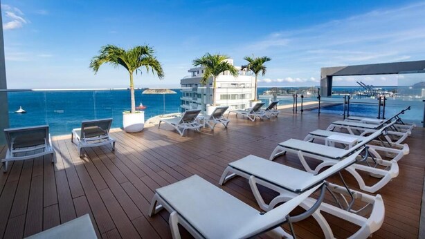 Um terraço com espreguiçadeiras e palmeiras com vista para o mar.