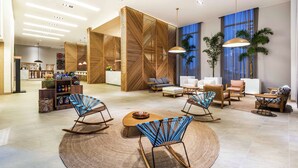 Um hall de hotel moderno, com área de estar central, divisórias de madeira e vista da cidade através de grandes janelas.