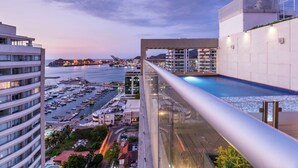 Um edifício alto com piscina no terraço e vista para uma marina e porto.