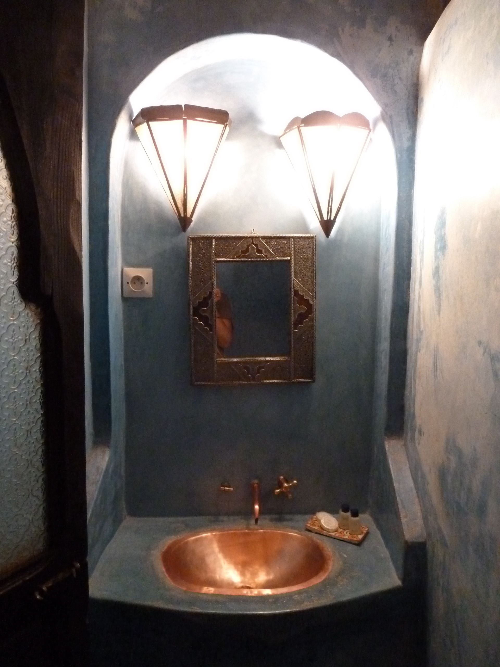 Casa de banho com lavatório de cobre, duas luzes embutidas na parede e um espelho.