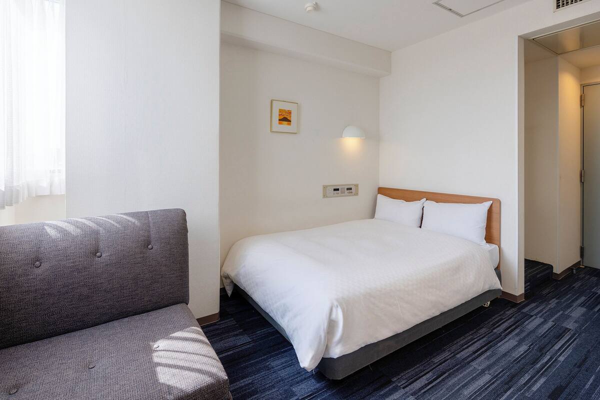 Quarto de hotel com cama, sofá, luminária na parede e um quadro.