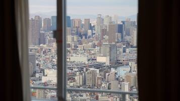Paisagem urbana visível através de uma janela, com edifícios de diferentes alturas e céu claro.