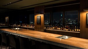 Um bar com balcão extenso, vários bancos e vista para a cidade através de grandes janelas.