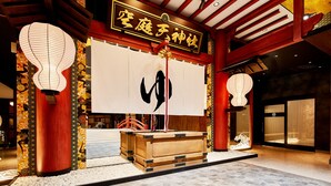 Um edifício japonês tradicional com estrutura de madeira, um grande lanterna de papel branca e uma placa com caracteres chineses.