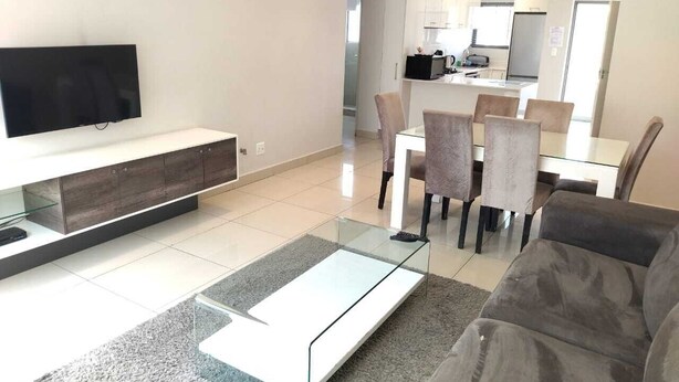 Uma sala de estar moderna com televisão de tela plana, uma mesa de centro de vidro e um sofá cinza.