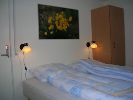 Quarto com cama, duas luminárias na parede, guarda-roupa de madeira e um quadro com flores amarelas.