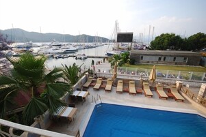 Área de piscina no terraço com espreguiçadeiras e vista para uma marina com barcos.