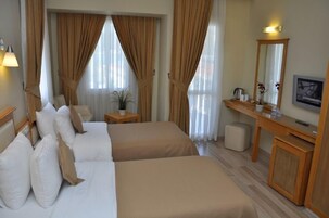 Quarto de hotel com duas camas, uma escrivaninha, uma cadeira, uma mesinha, um espelho e uma janela com cortinas.