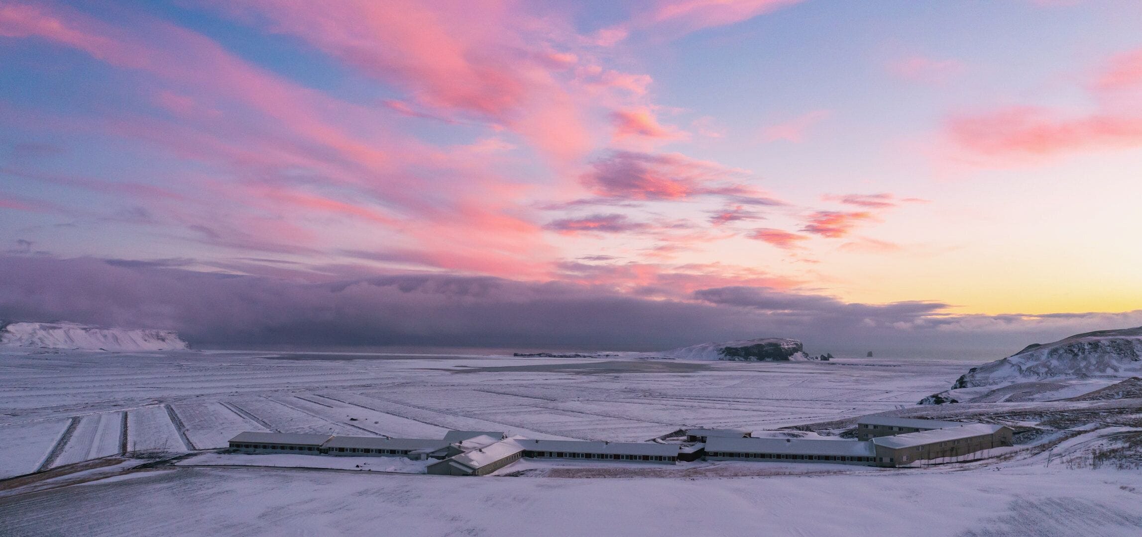 Paisagem coberta de neve com um conjunto de edifícios e um vasto campo aberto.