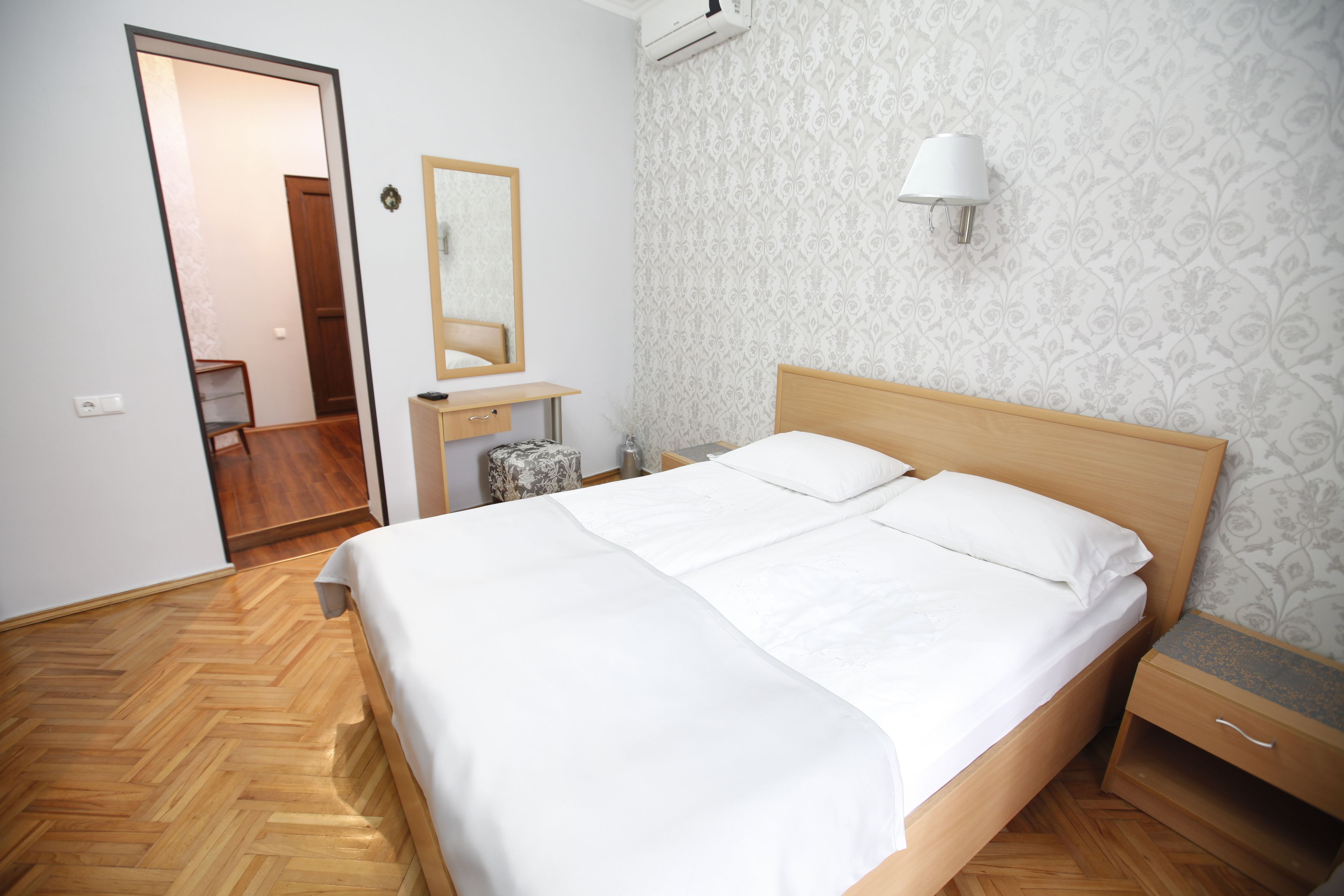 Quarto bem organizado com cama de madeira, mesa de cabeceira, espelho e luminária na parede.