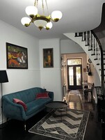 Uma sala de estar com um sofá verde-água, um candelabro e duas pinturas na parede.