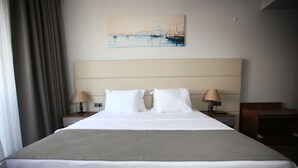 Quarto de hotel com uma cama grande, duas mesas de cabeceira com luminárias, um quadro na parede e uma janela com cortinas.