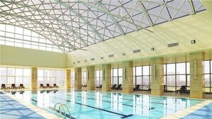 Piscina interna com paredes de vidro transparente, grandes janelas e teto alto.
