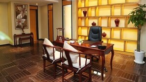 Uma sala de conferências com uma mesa de madeira, cadeiras, uma escrivaninha e uma estante com objetos decorativos.