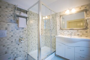 Um banheiro com chuveiro em box de vidro, pia branca com espelho e parede revestida com azulejos.