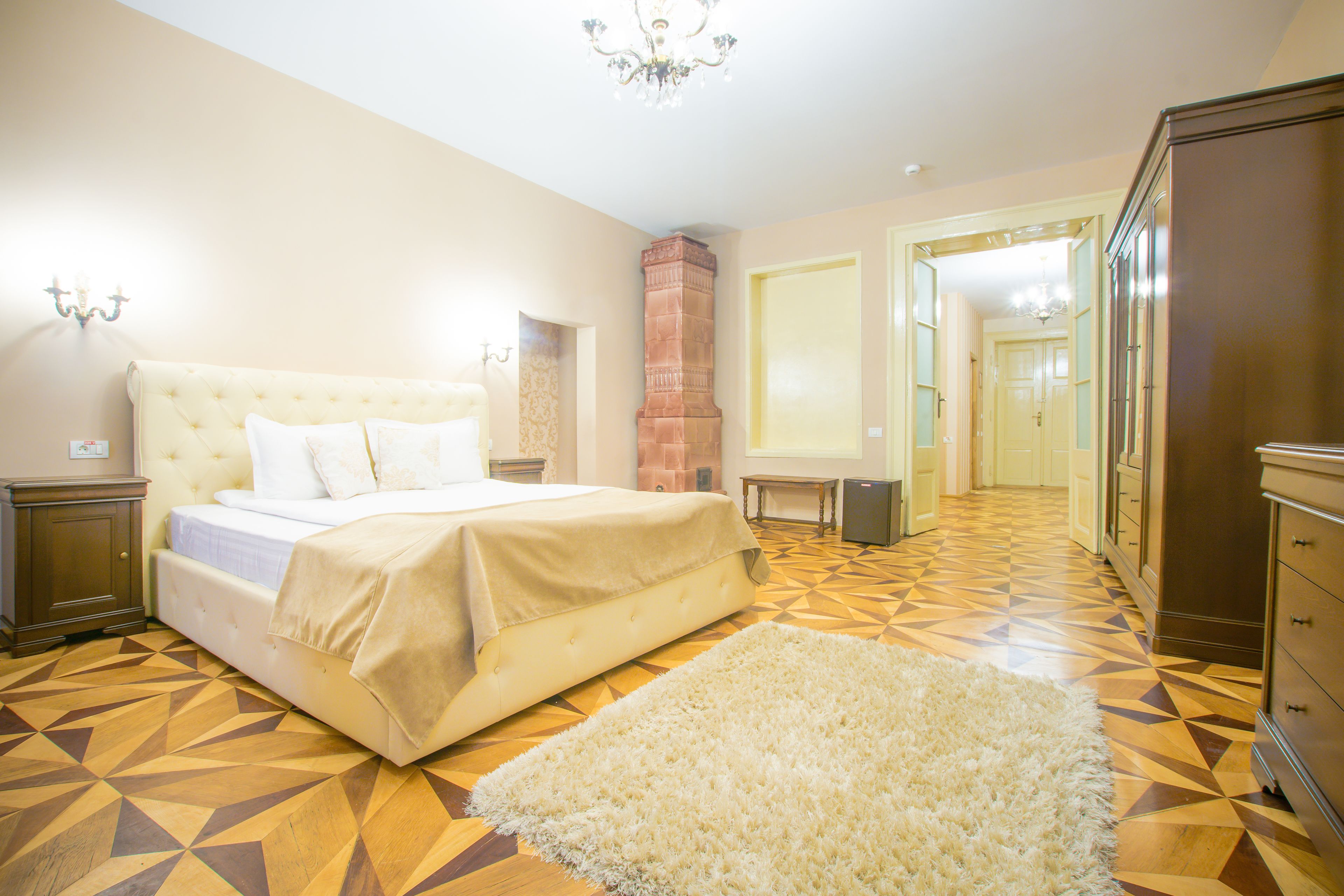 Quarto com uma cama grande, um candelabro, piso estampado e um guarda-roupa de madeira.