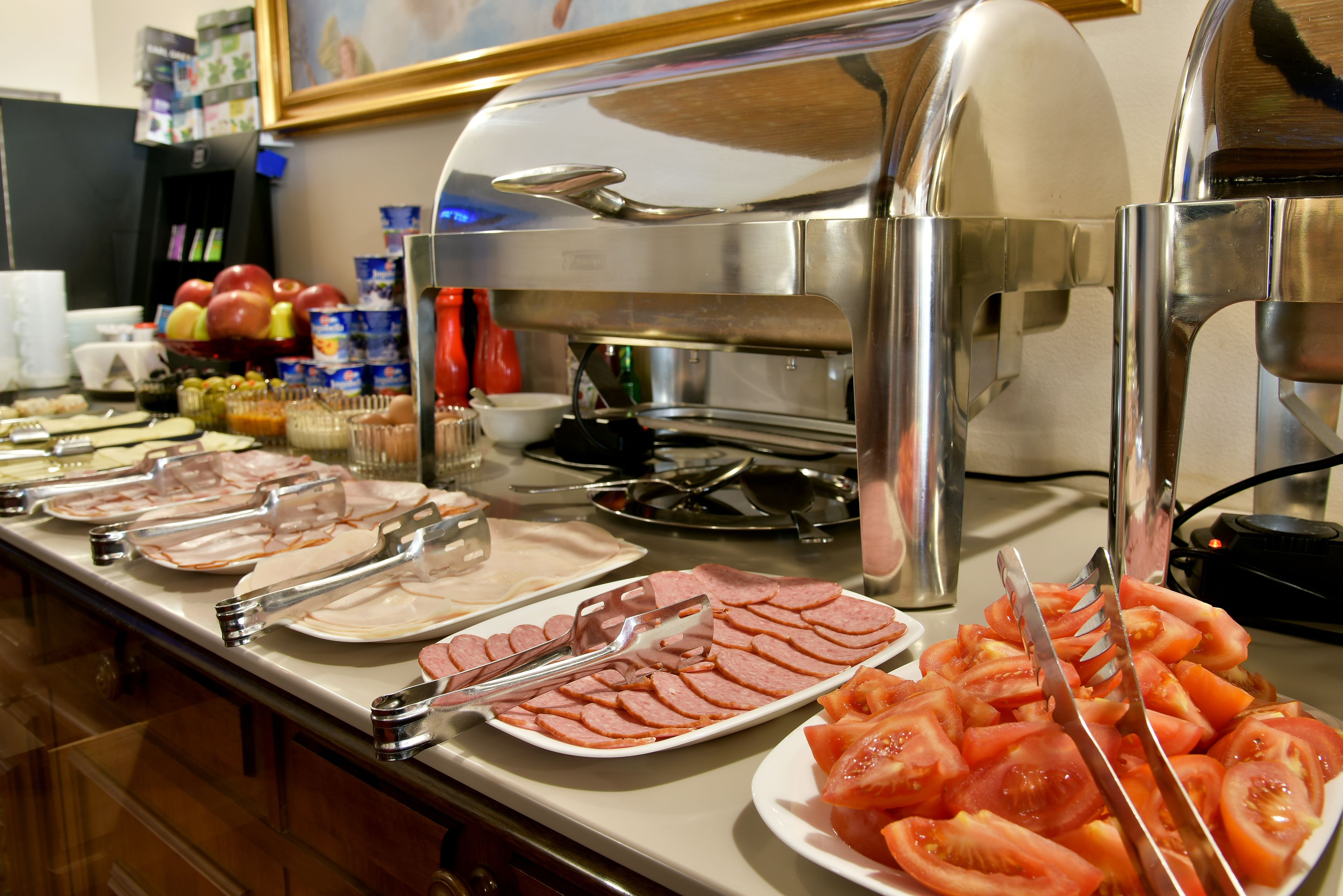 Buffet com diversos alimentos, incluindo presunto fatiado e tomates.