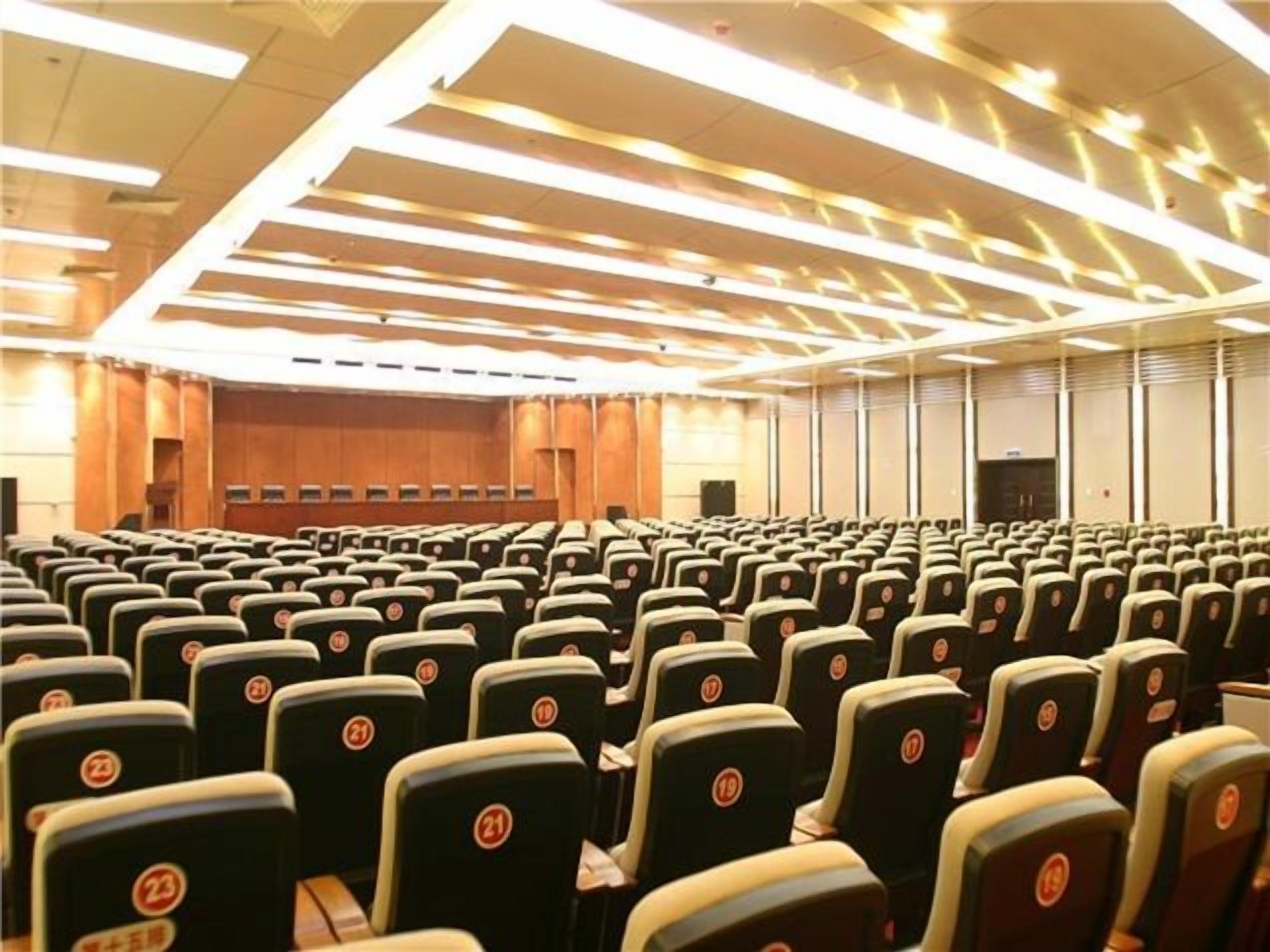 Sala de conferência com fileiras de cadeiras, palco e design moderno no teto.