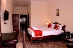 Quarto de hotel com cama de madeira, uma escrivaninha, uma cadeira, televisão e um quadro na parede.