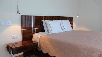 Quarto moderno com cabeceira de madeira, mesa de cabeceira e cama com colcha bege.