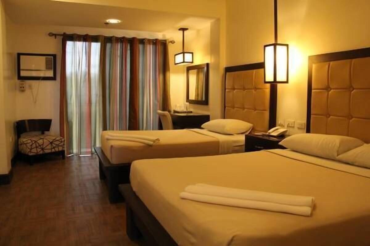 Quarto de hotel com duas camas, uma escrivaninha, uma cadeira e uma janela com cortinas.