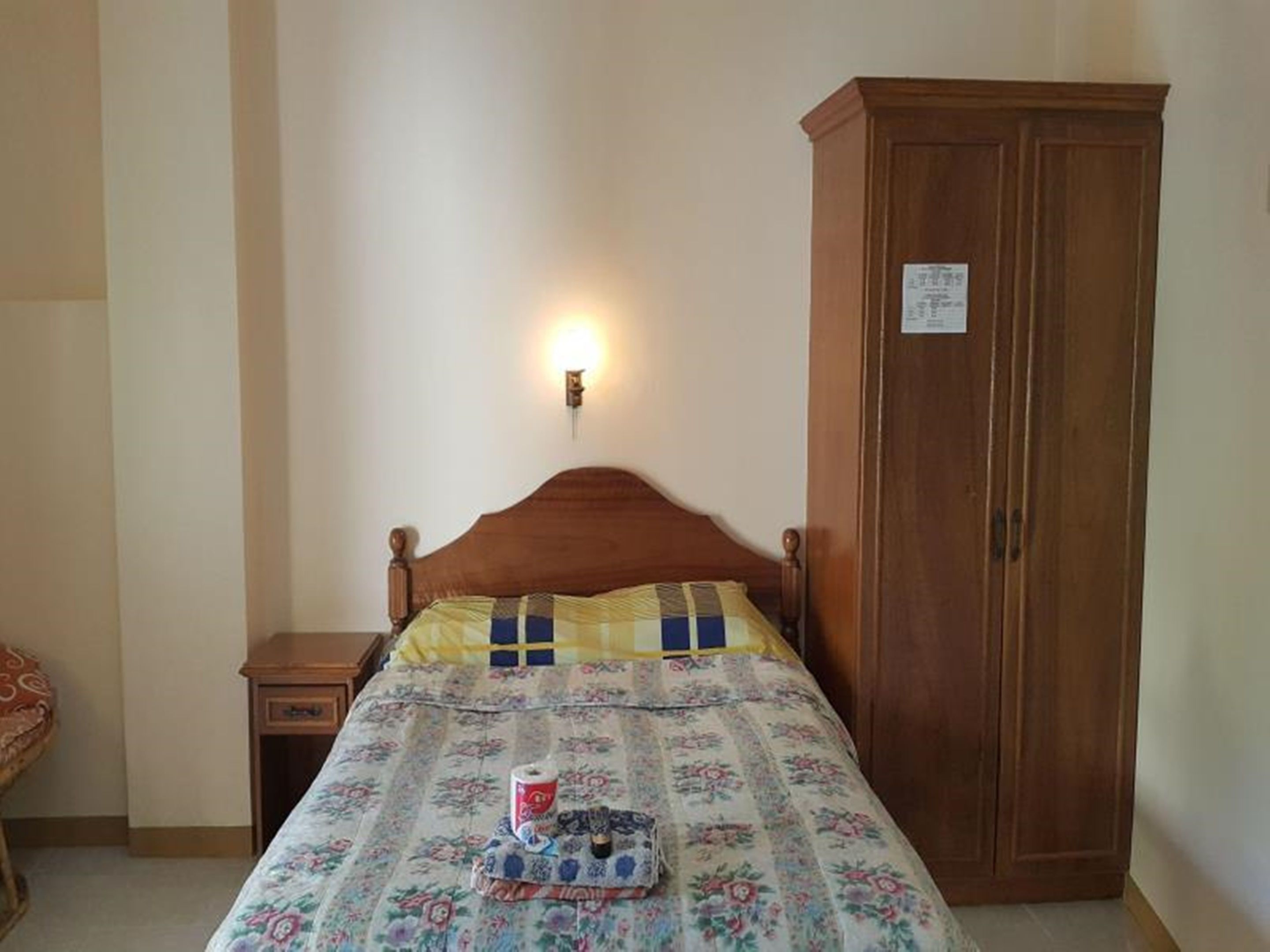 Quarto com cama de madeira, mesa de cabeceira, guarda-roupa e luminária na parede.