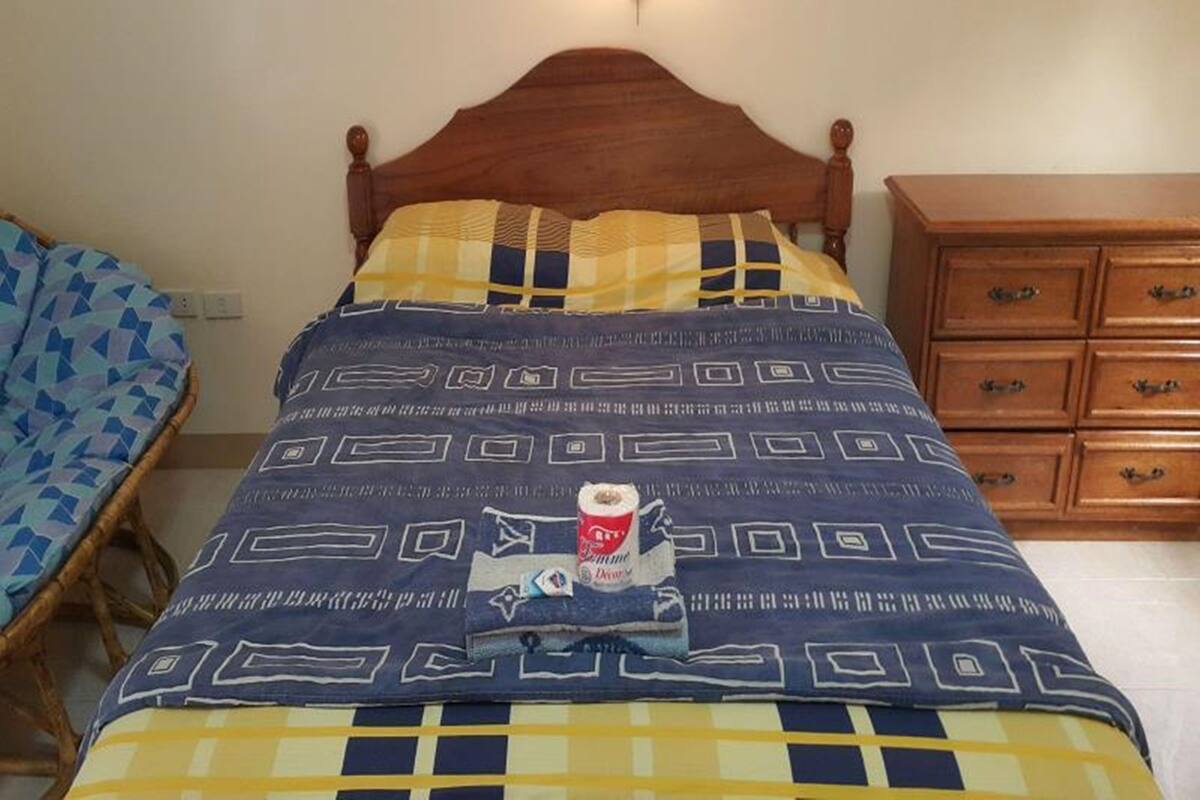 Quarto com cabeceira de madeira, colcha estampada, mesa de cabeceira com gavetas e cadeira de vime.
