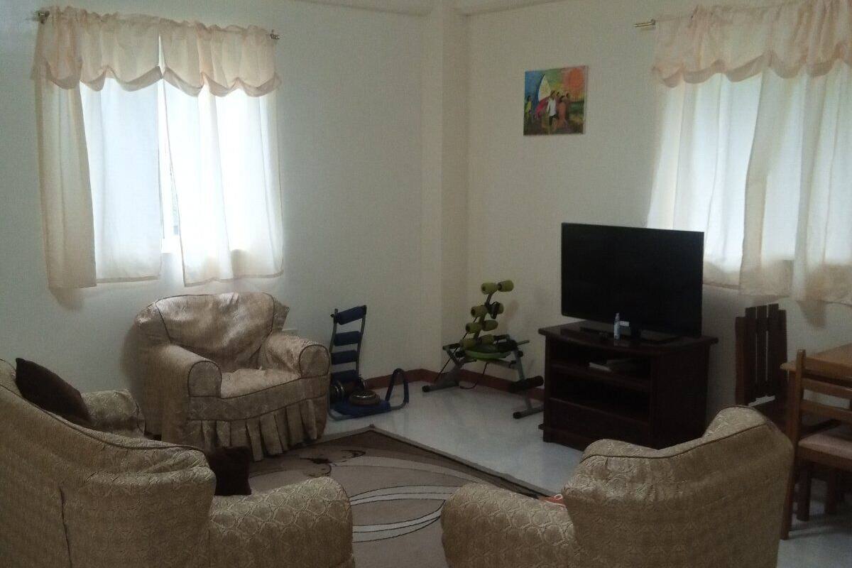 Sala de estar com poltronas bege, uma televisão e uma mesinha.