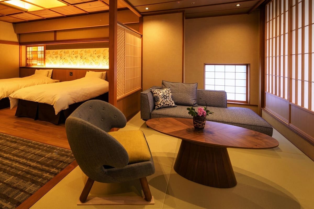 Quarto em estilo japonês tradicional, com duas camas, um sofá, uma poltrona e uma mesinha de centro com um vaso.