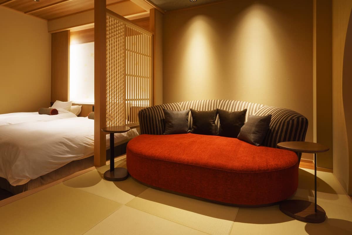 Um quarto tradicional japonês com tatame, cama de madeira baixa, sofá com almofadas, uma pequena mesa e uma porta de correr.