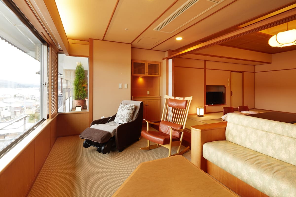 Quarto de hotel compacto com sofá, cadeira de balanço, pequena mesa e televisão.