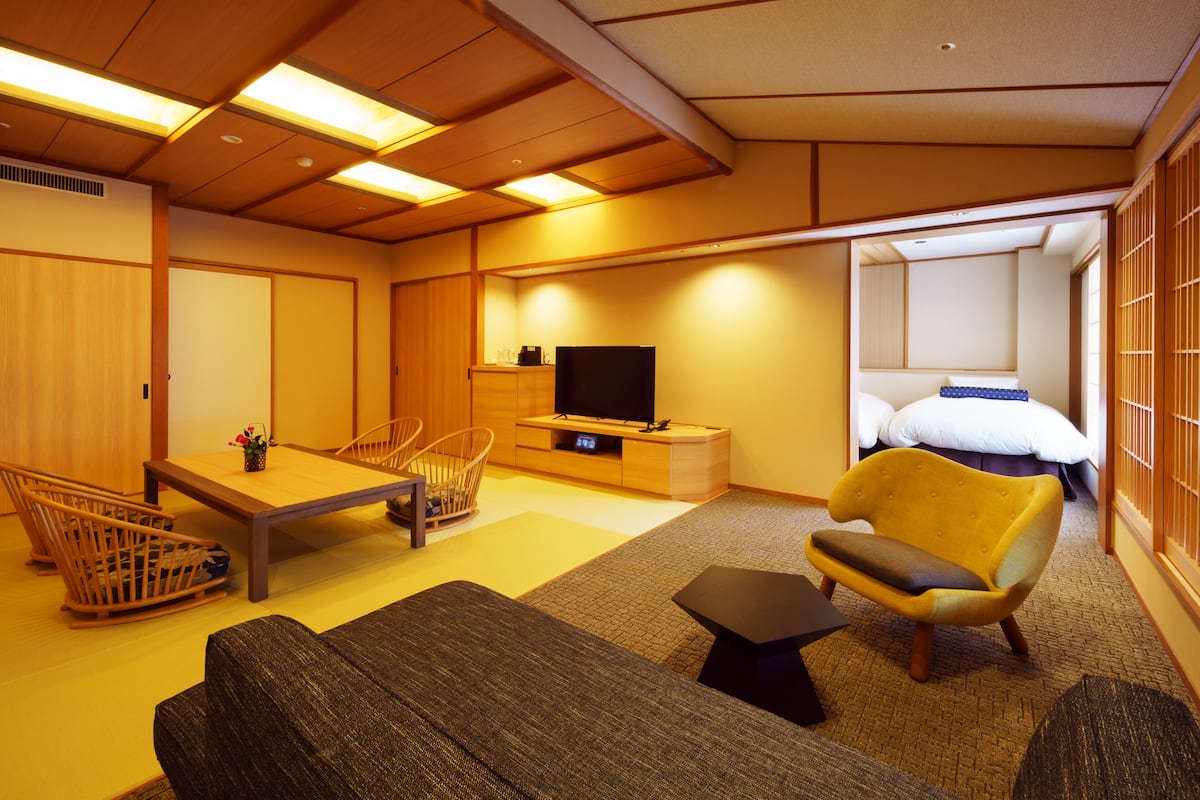 Um quarto em estilo japonês tradicional, com tatames, uma mesa de madeira baixa, um sofá, uma televisão e uma futon.