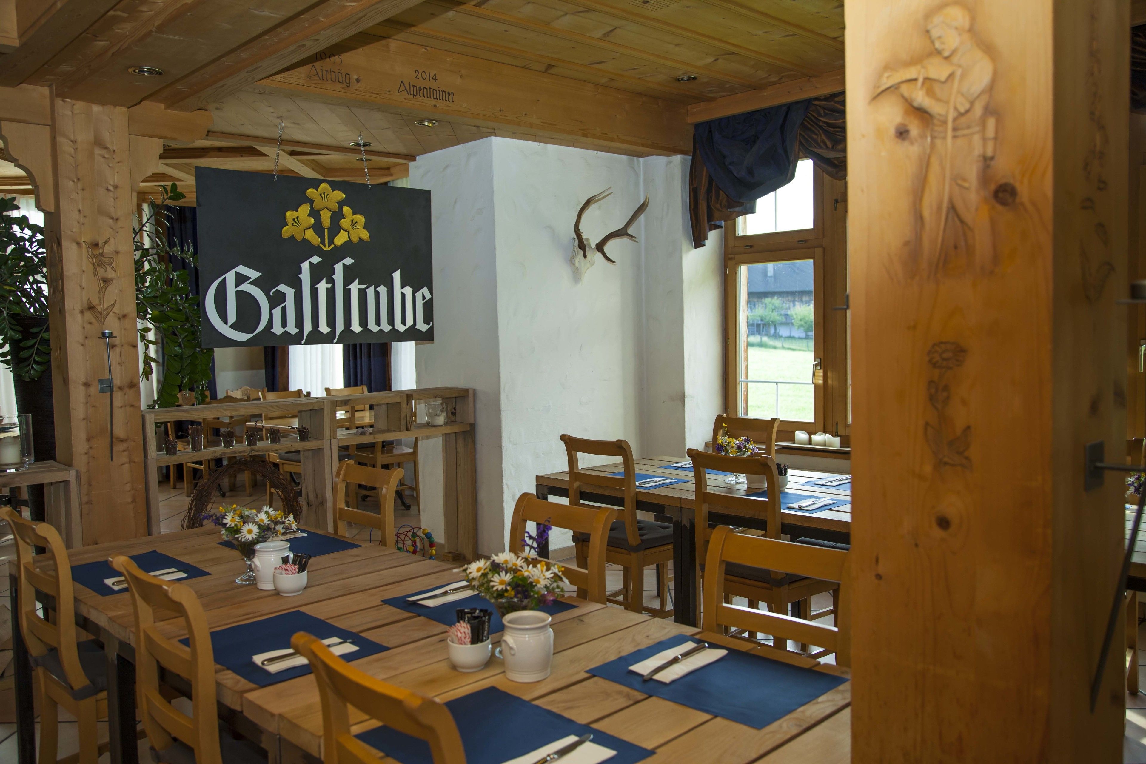 Uma área de refeições de madeira com mesas postas para quatro, uma placa com a inscrição "Galthube" e uma cabeça de veado montada na parede.