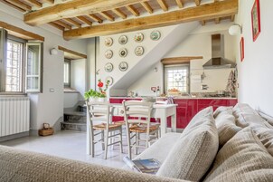 Uma sala de estar acolhedora com um sofá, um espaço de jantar com mesa e cadeiras, uma cozinha com armários vermelhos e uma escada que leva a outro andar.
