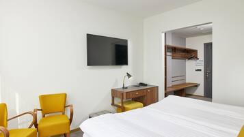 Quarto de hotel com uma cama, uma escrivaninha com cadeira, televisão e guarda-roupa.