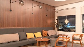 Sala de estar moderna com sofá cinza, detalhes em madeira e vista para a cidade à noite.