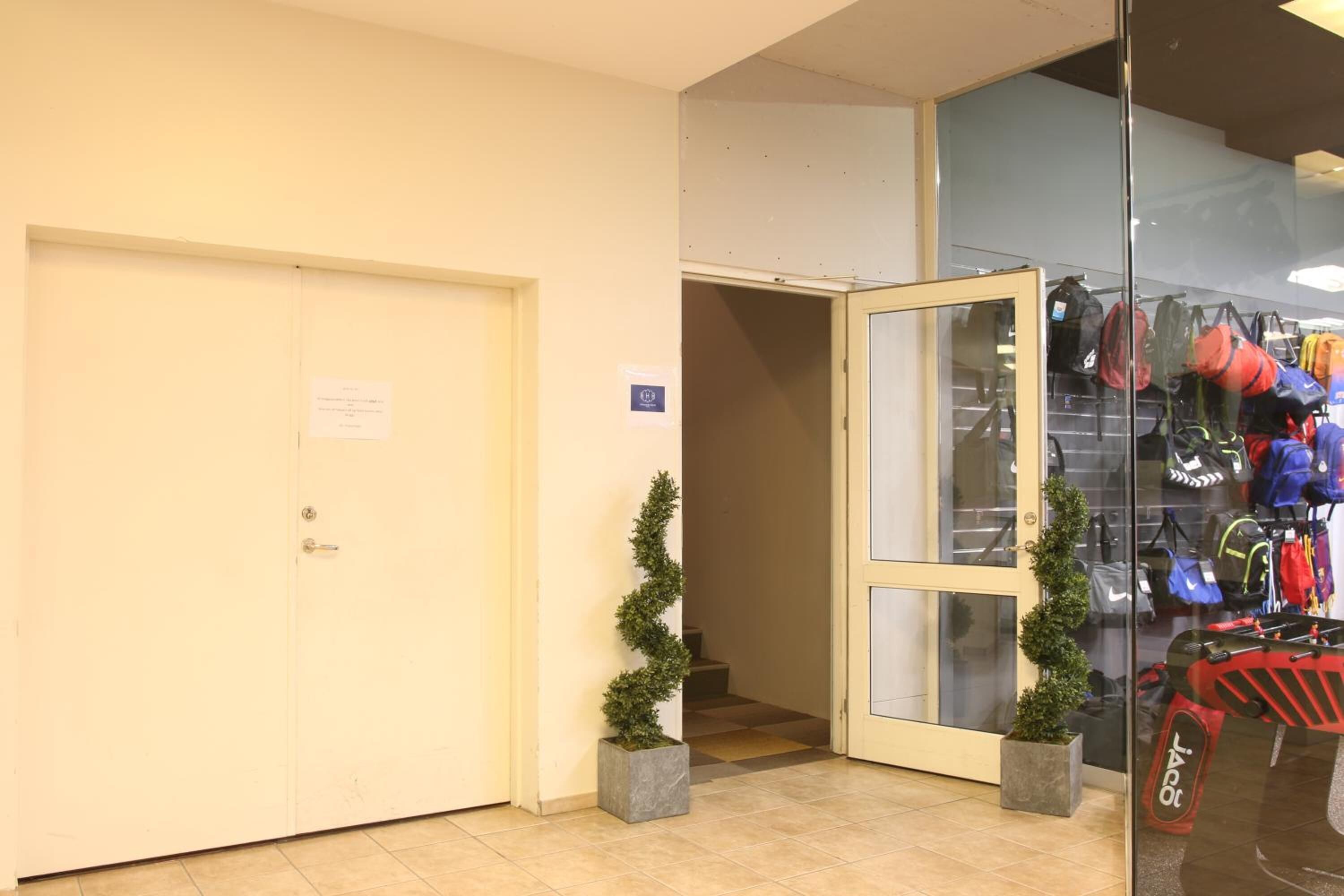 Um saguão de hotel com uma porta fechada, uma porta de vidro que dá para um quarto e uma exposição de malas esportivas.