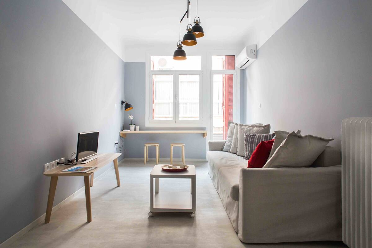 Uma sala de estar moderna com um sofá, uma mesa de centro, uma escrivaninha com um computador e iluminação pendente.