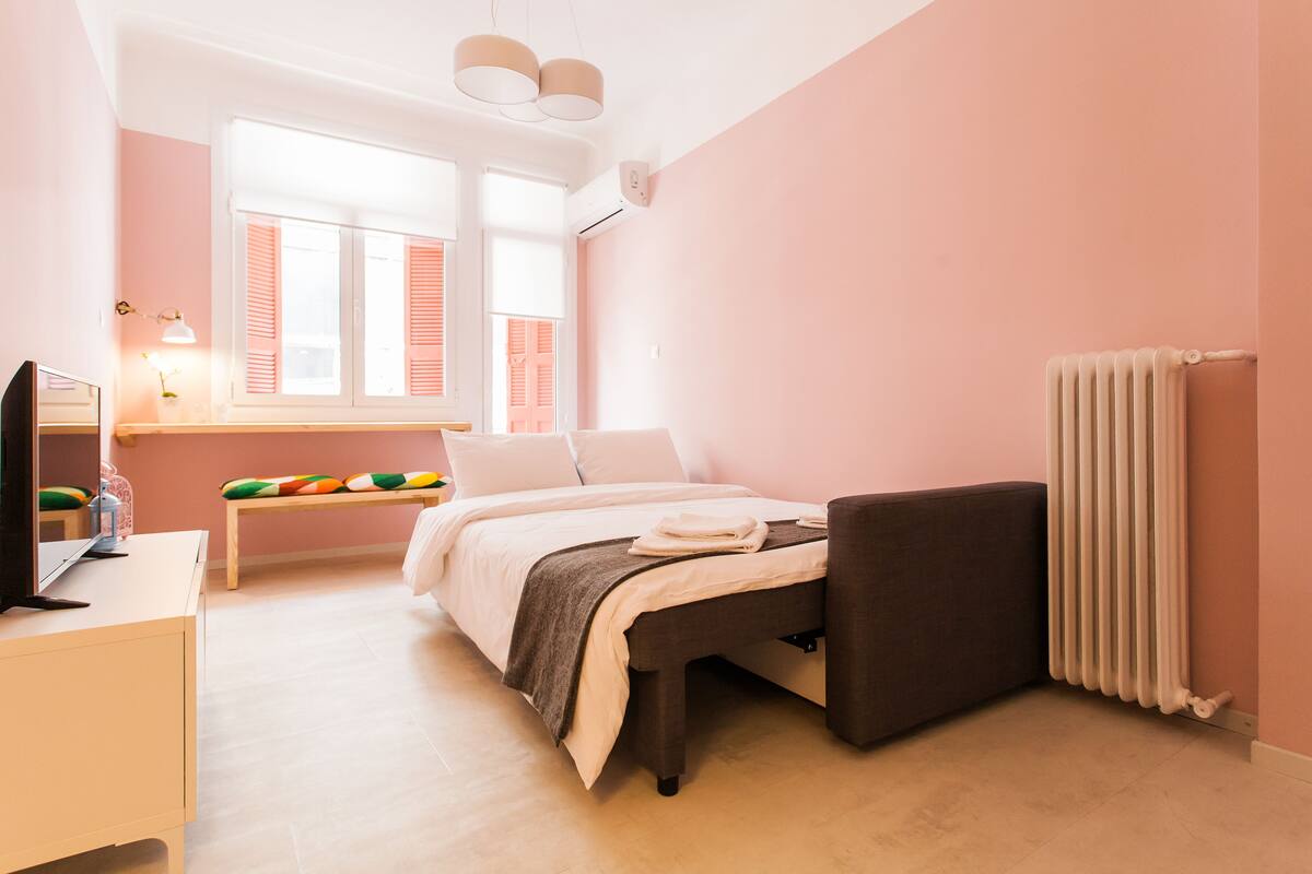 Quarto com cama, mesa de cabeceira, luminária e janela com persianas.