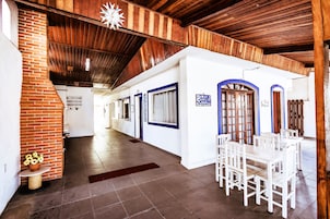 Um corredor espaçoso com teto de madeira, paredes brancas e uma parede de tijolos de um lado. Há uma área de refeições com cadeiras e mesa brancas.