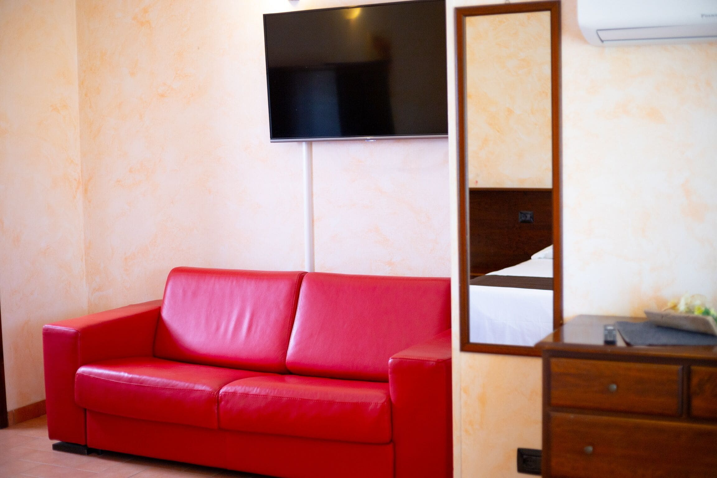 Um sofá vermelho, uma TV fixada na parede e um aparador de madeira com espelho.