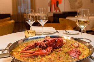 Prato de frutos do mar com lagosta sobre uma cama de arroz, acompanhado de copos de vinho em uma mesa.