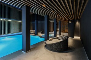 Uma área interna de piscina moderna com um espaço de estar circular, hidromassagem e espreguiçadeiras junto à piscina.