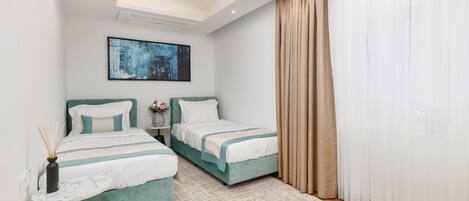 Quarto de hotel moderno com duas camas, uma mesa pequena, um vaso com juncos e um quadro abstrato grande na parede.