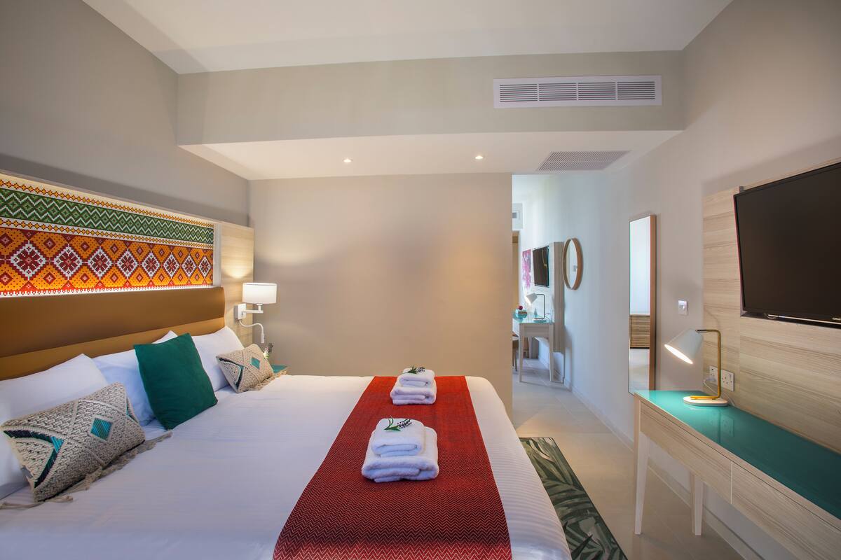 Quarto de hotel com uma cama grande, televisão, escrivaninha e banheiro visível por uma porta aberta.