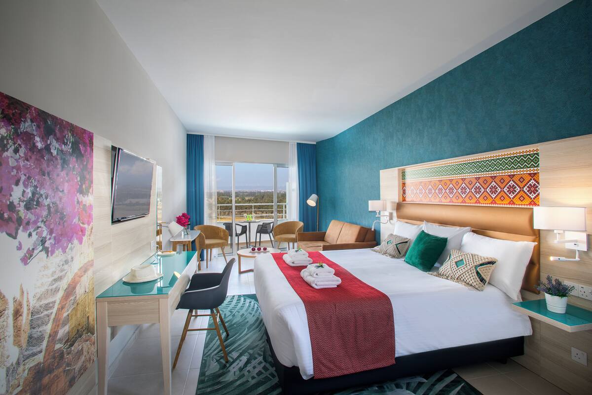 Quarto de hotel com uma cama grande, uma escrivaninha, uma cadeira, uma mesinha e vista para a cidade.