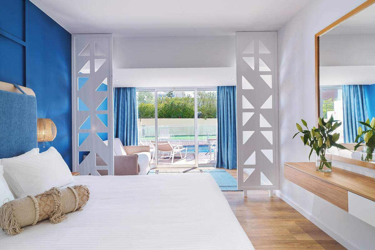 Quarto de hotel moderno com uma cama grande, uma varanda com área de estar ao ar livre e vista para a piscina.