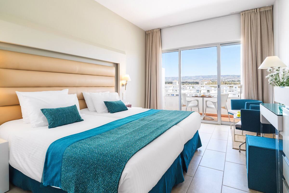 Quarto de hotel com uma cama grande, uma escrivaninha com cadeira e varanda com vista.