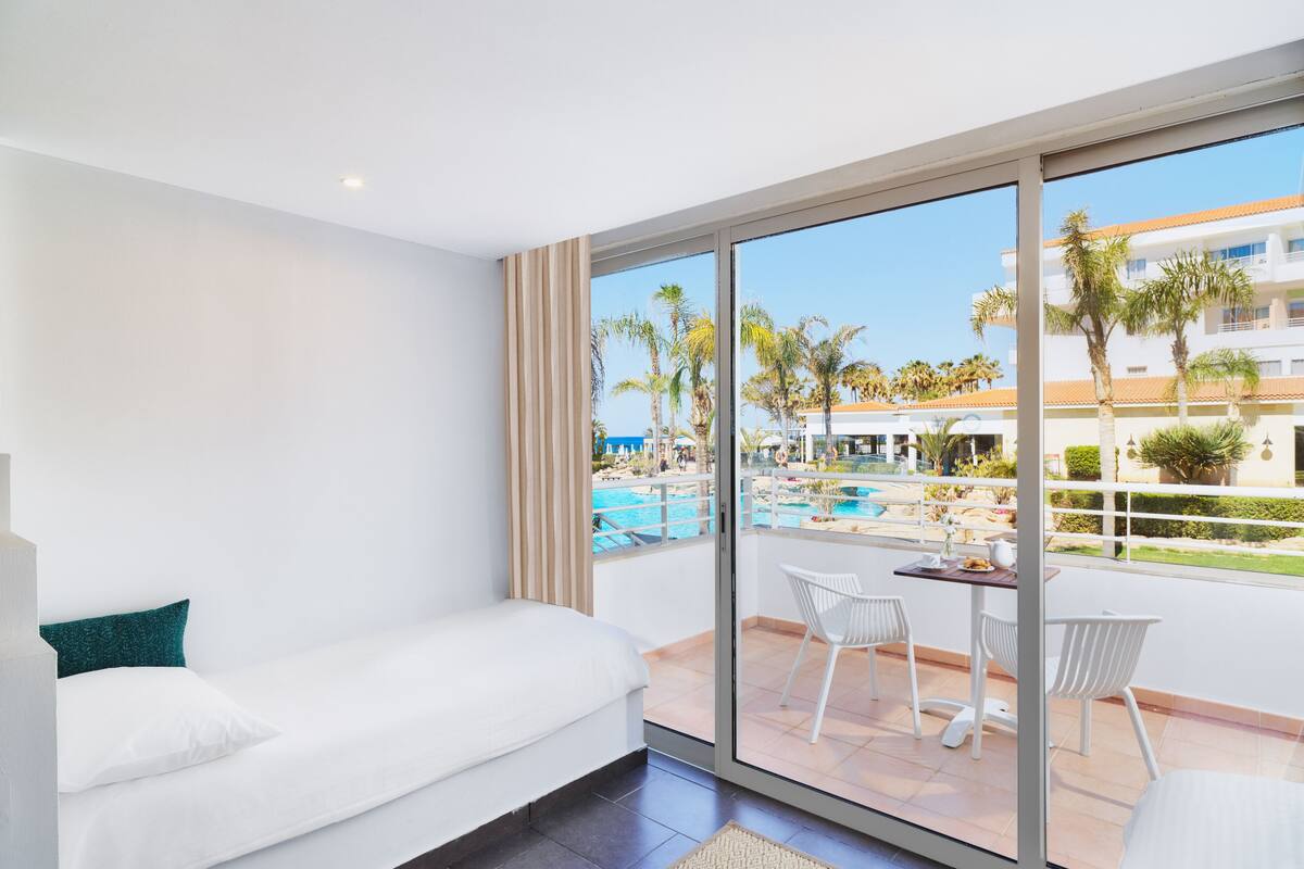 Quarto de hotel moderno com varanda, vista para a piscina e um sofá branco.