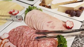 Buffet com diversos alimentos, incluindo carnes fatiadas, queijos e legumes.